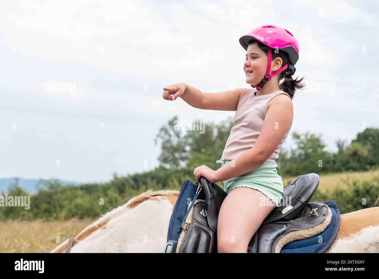 A young girl, joyfully riding a horse, points towards the horizon. She ...