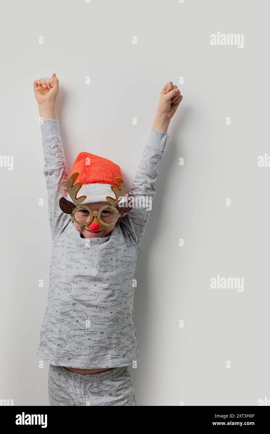 A joyful child wearing a reindeer mask, Santa hat, and glasses raises ...