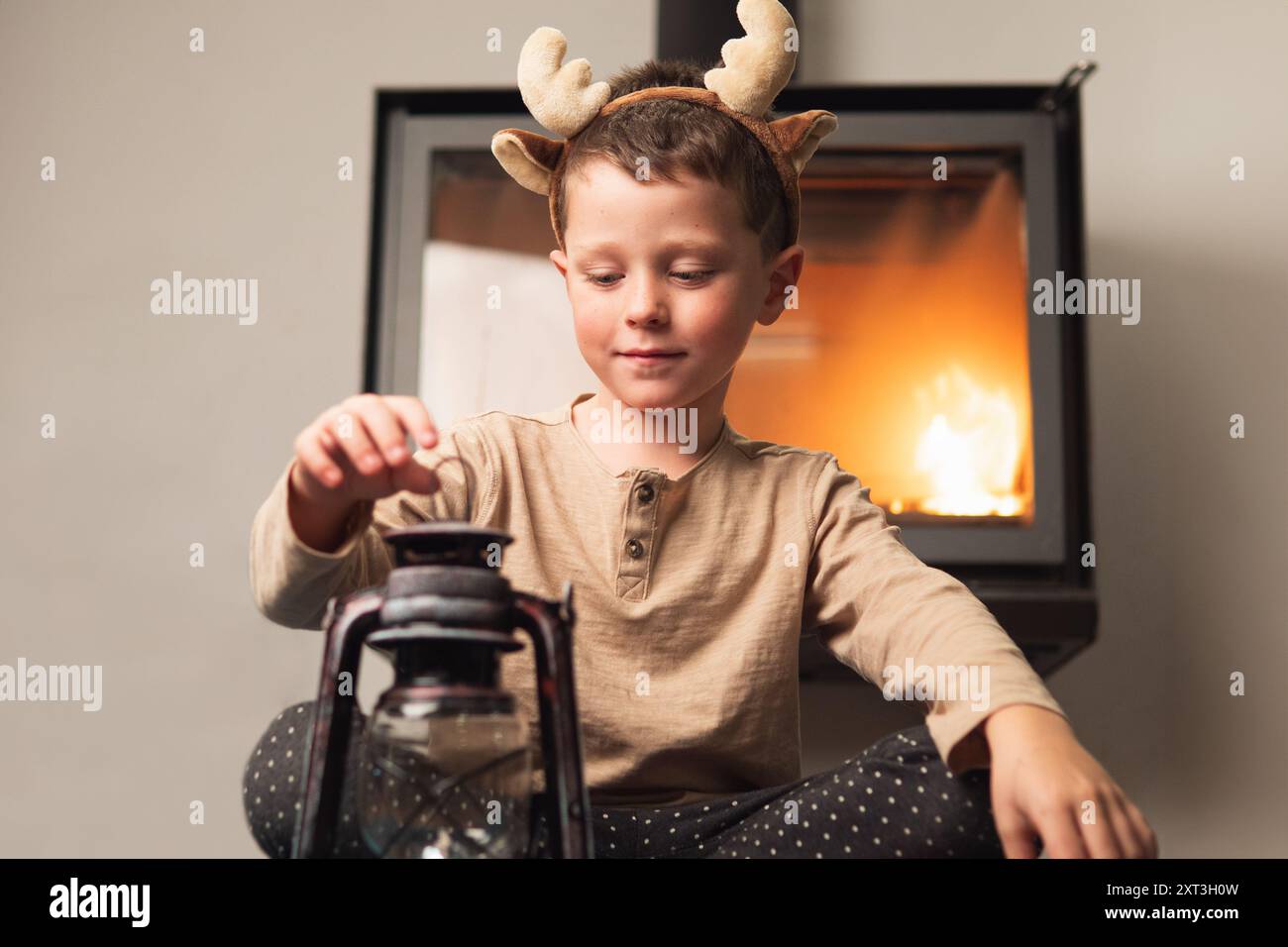 A young boy wears reindeer antlers while playing with a lantern by the ...