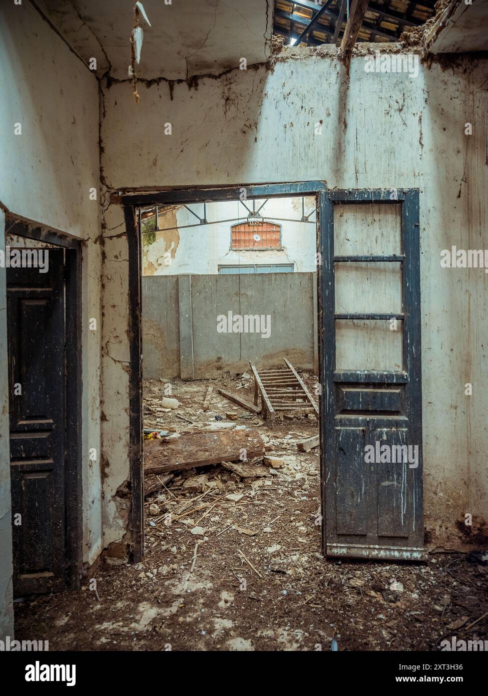 A hauntingly empty room in an abandoned building, with peeling paint, debris, and a collapsed ...