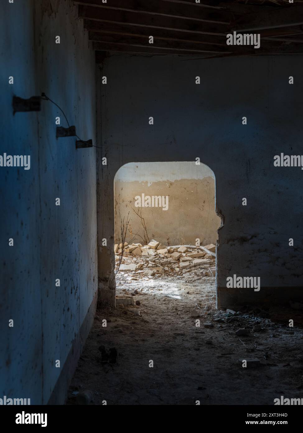 A beam of sunlight streams through an arched doorway in a desolate ...