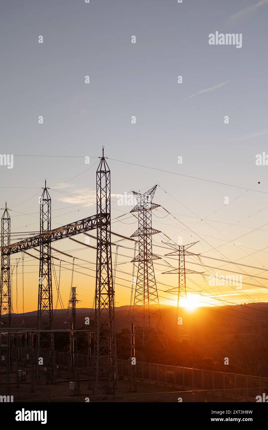 Golden sunset behind a labyrinth of power lines and towers at a ...