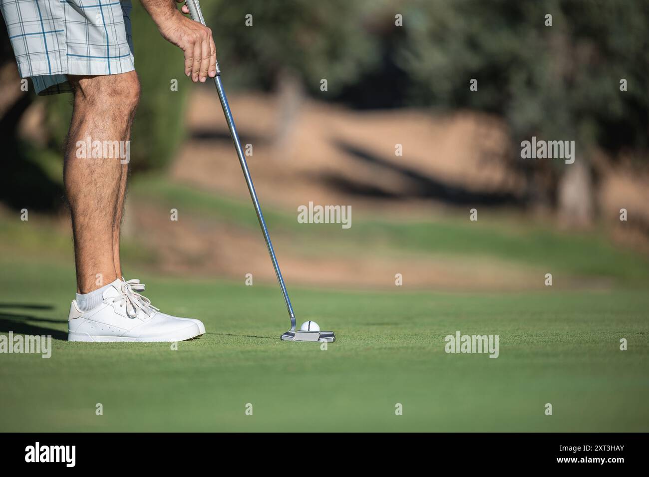 Cropped close-up of an unrecognizable male golfer's legs and putter ...