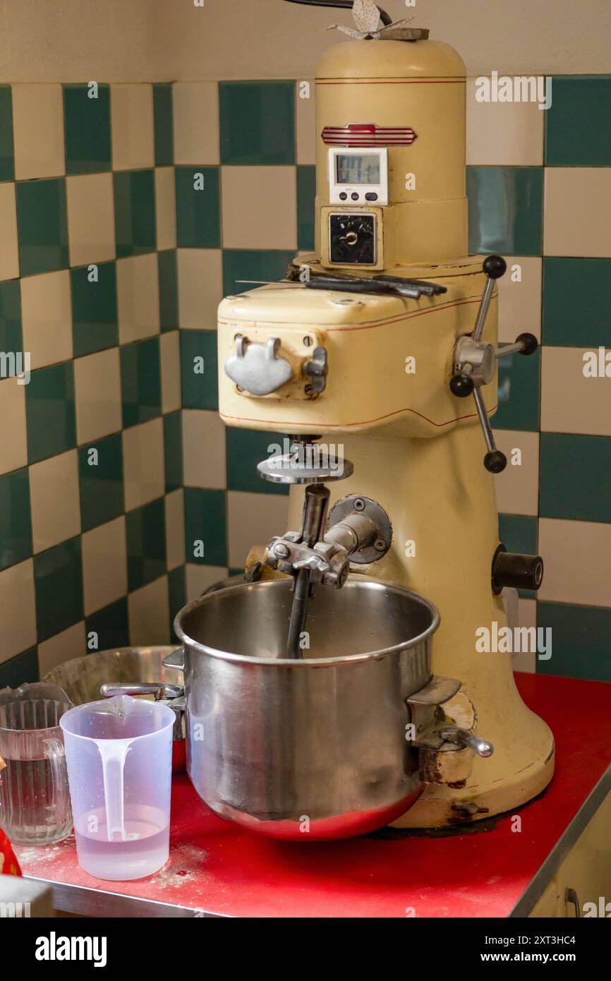 An aged dough mixer stands on a red tabletop, backed by green and cream ...
