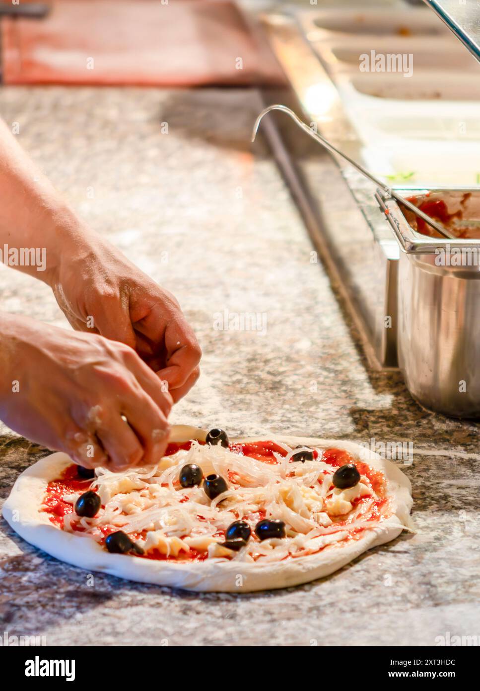 A close-up image showing a chef's hands topping a pizza with mozzarella ...