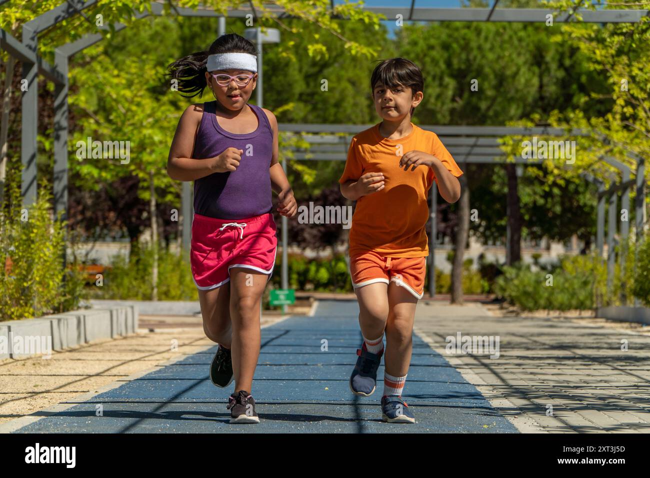Two multiethnic children, a girl and a boy, are jogging together in a ...