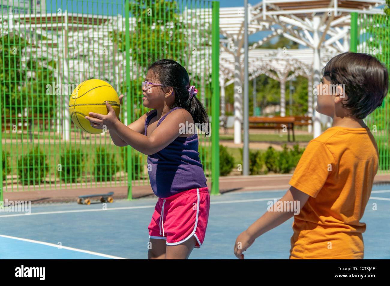 Two multiethnic children engage in a playful basketball game on a sunny ...