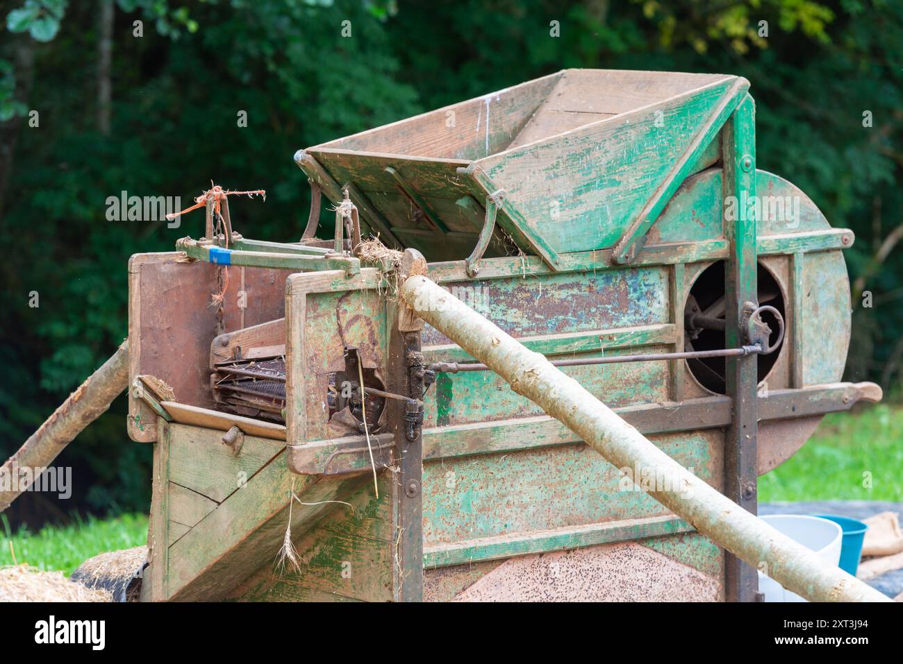 An old, worn wheat thresher, in a green, wooded area, shows the ancient ...