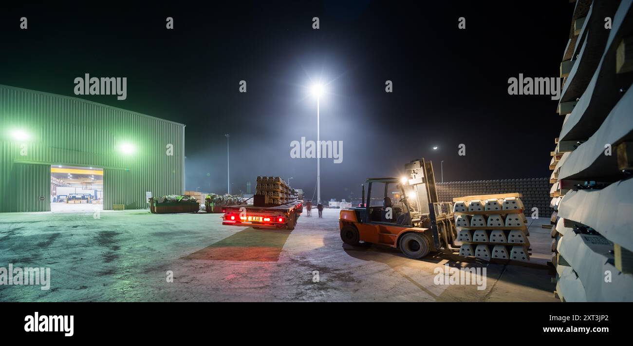 Industrial night setting with forklift loading railway sleepers onto a ...