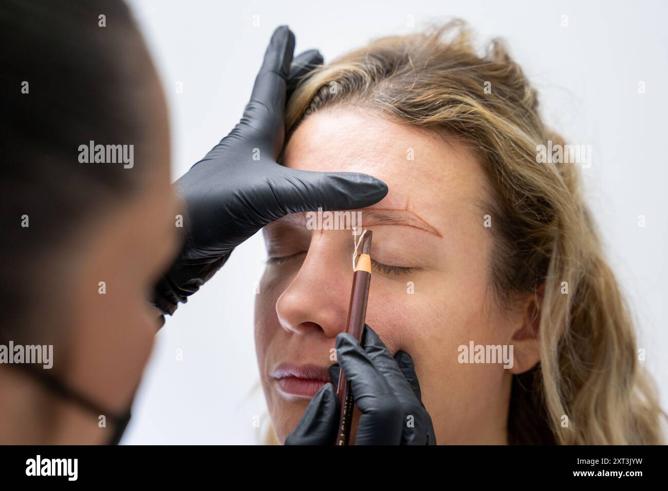 This image captures a beautician mapping out the eyebrows of a client ...