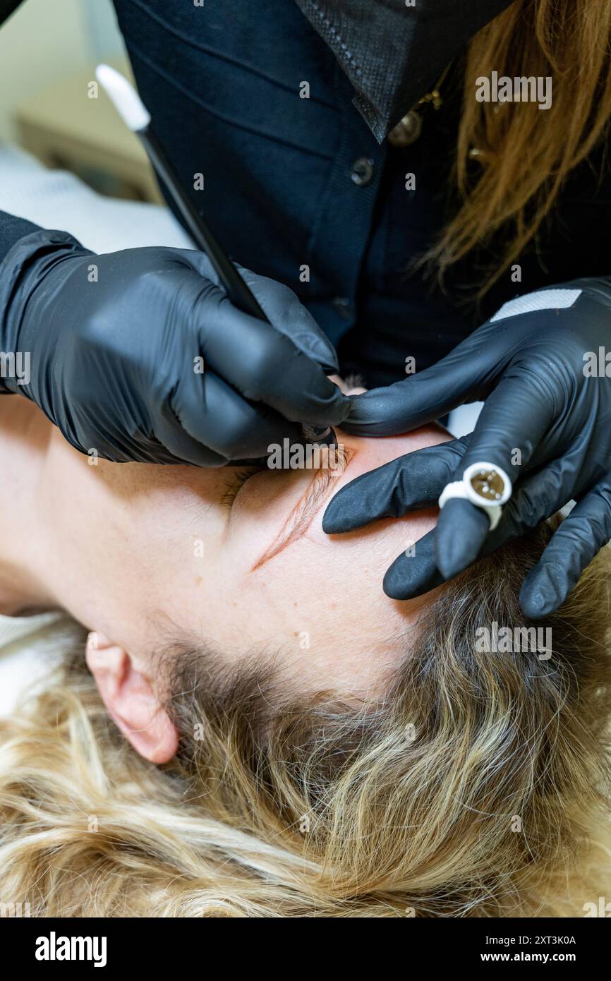 This image captures a beautician meticulously performing a microblading ...