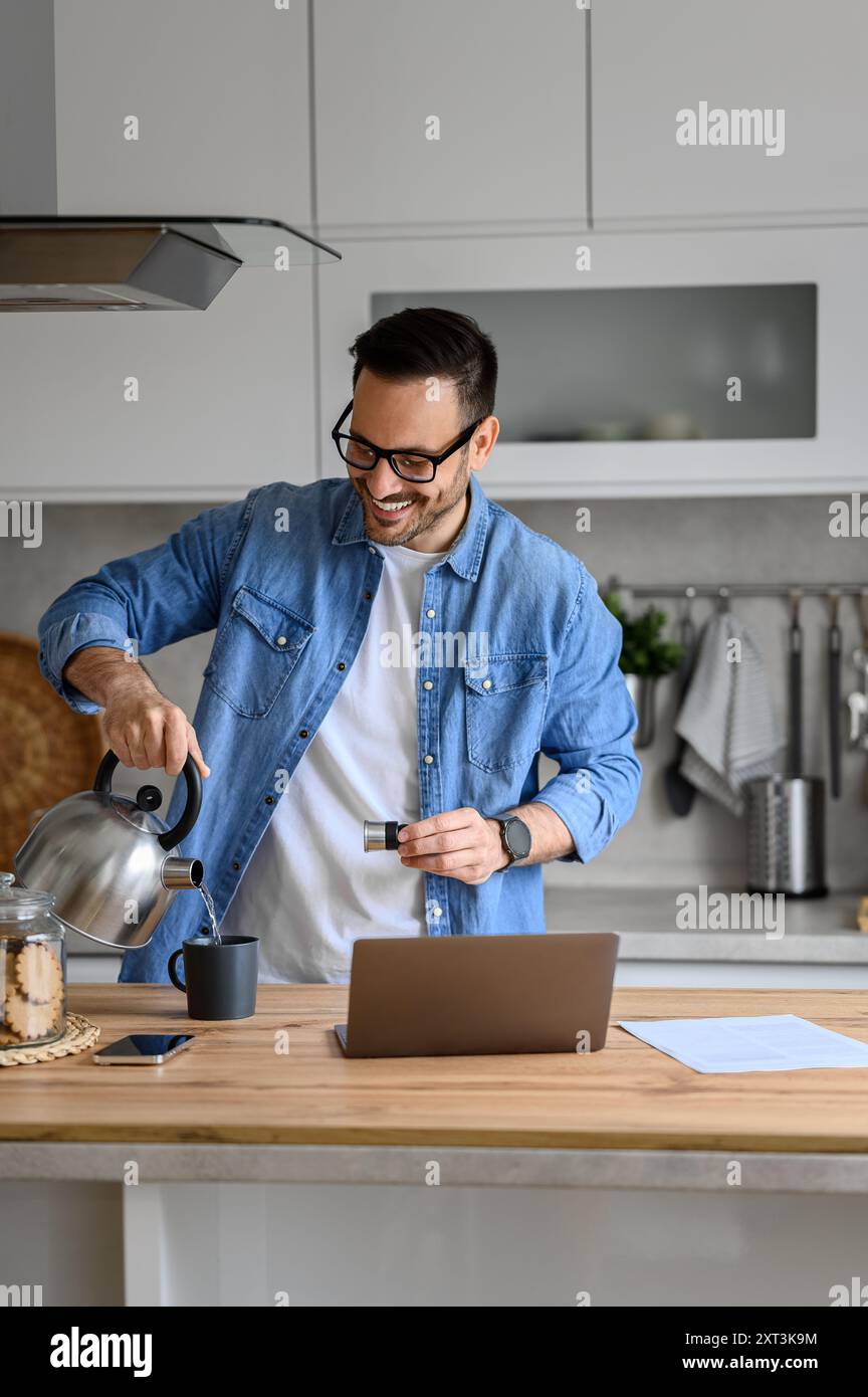 Smiling businessman pouring hot water in coffee cup while working over ...