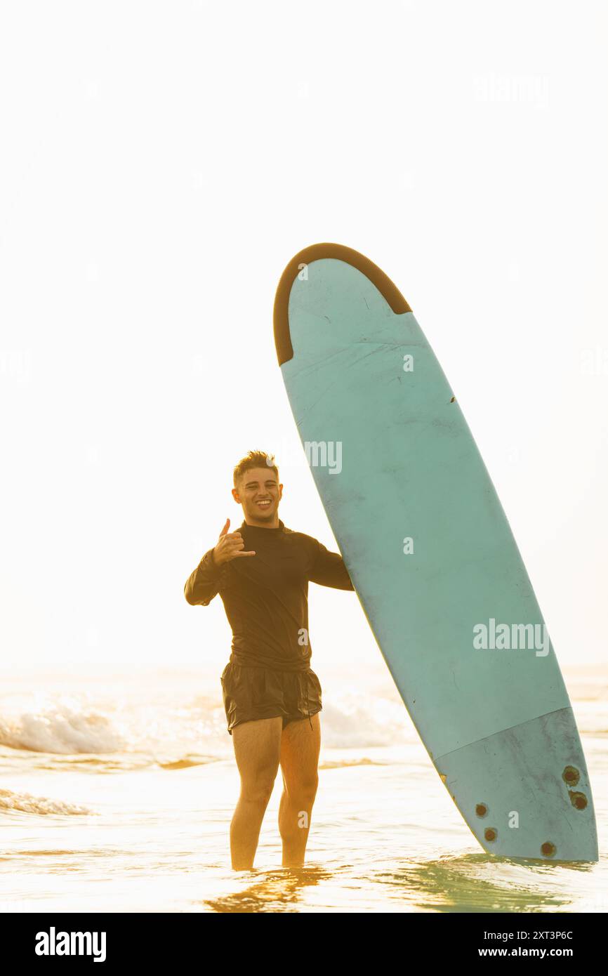 Happy surfer making hand gestures next to his surfboard Stock Photo - Alamy