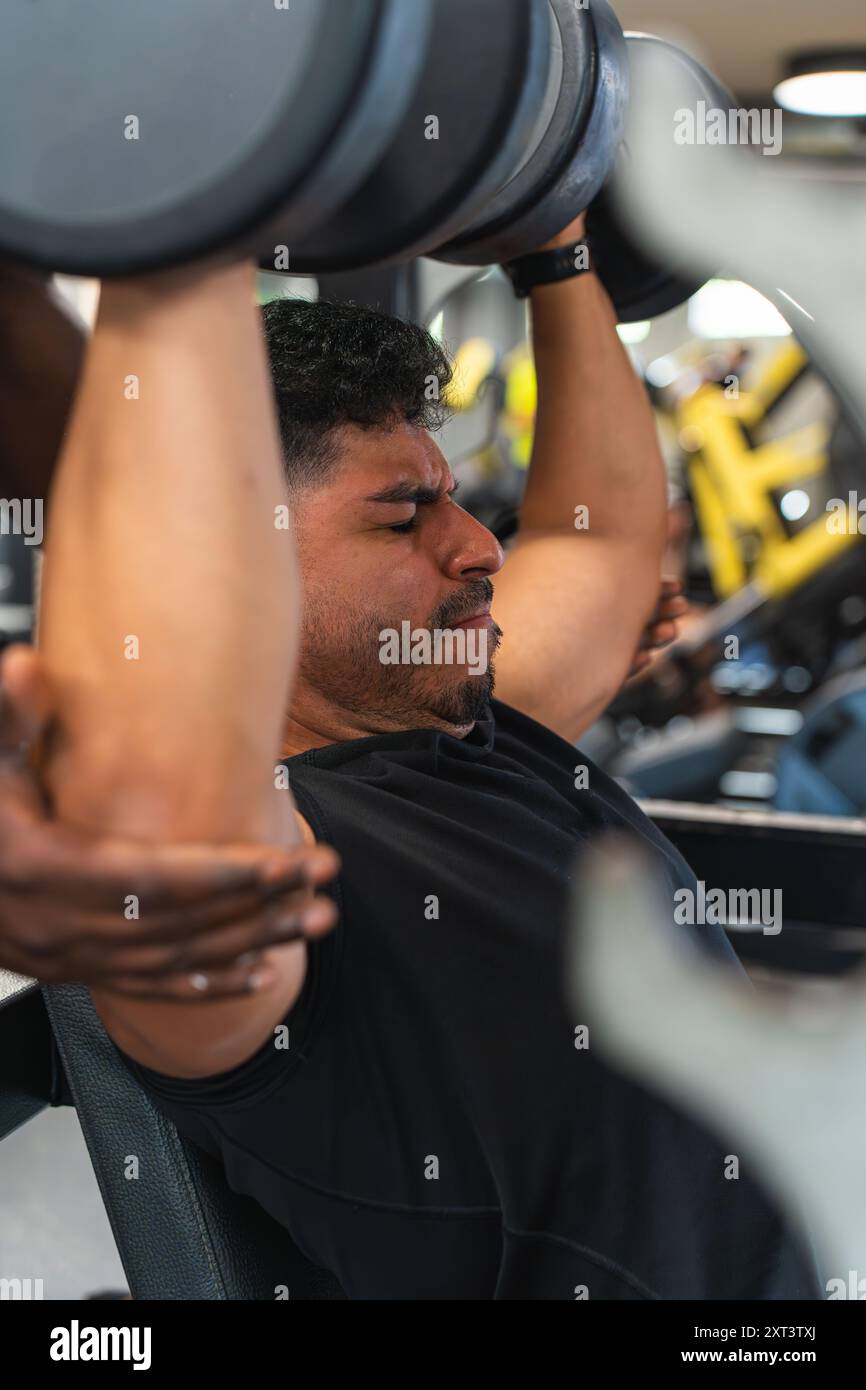 Young Latino man lifting weights at the gym with the help of his ...