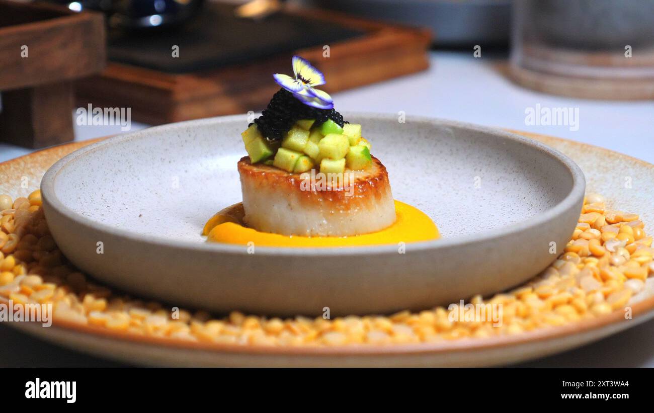 Gourmet dish of seared scallop with mango puree and avocado garnish in ...