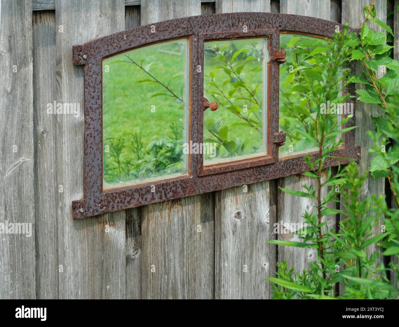 Rusty wrought iron window frame with mirror glass on a shed wall ...