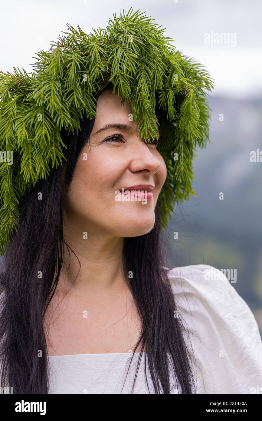 Portrait of smiling friendly Caucasian middle aged woman in head wreath of conifer needle tree ...