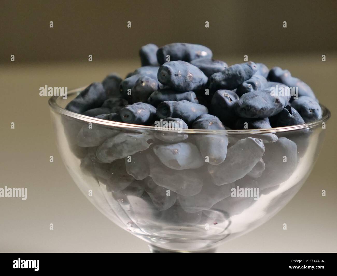 A close-up shot of a glass bowl filled with fresh, plump Honeyberries ...