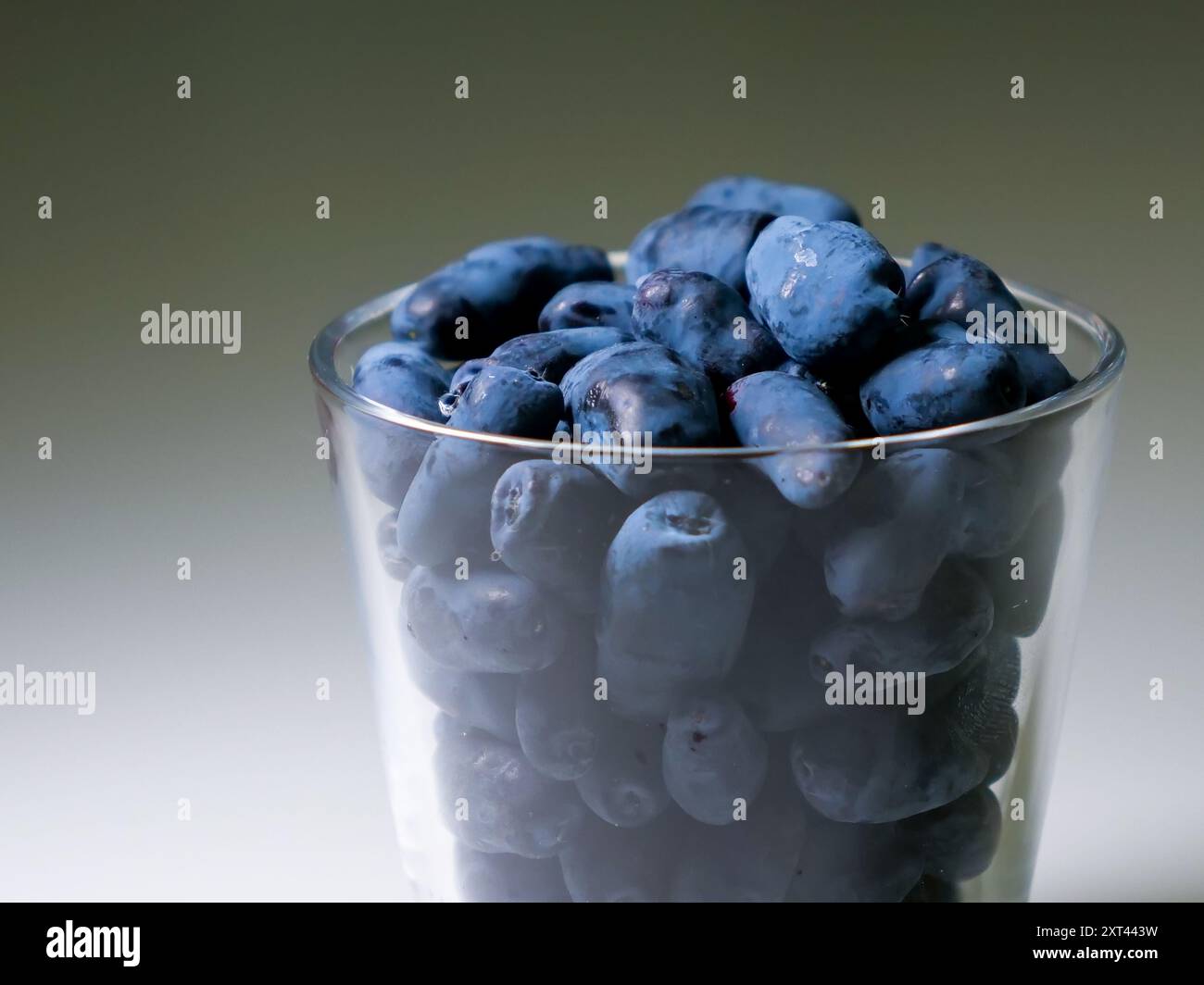 A close-up shot of a glass bowl filled with fresh, plump Honeyberries ...