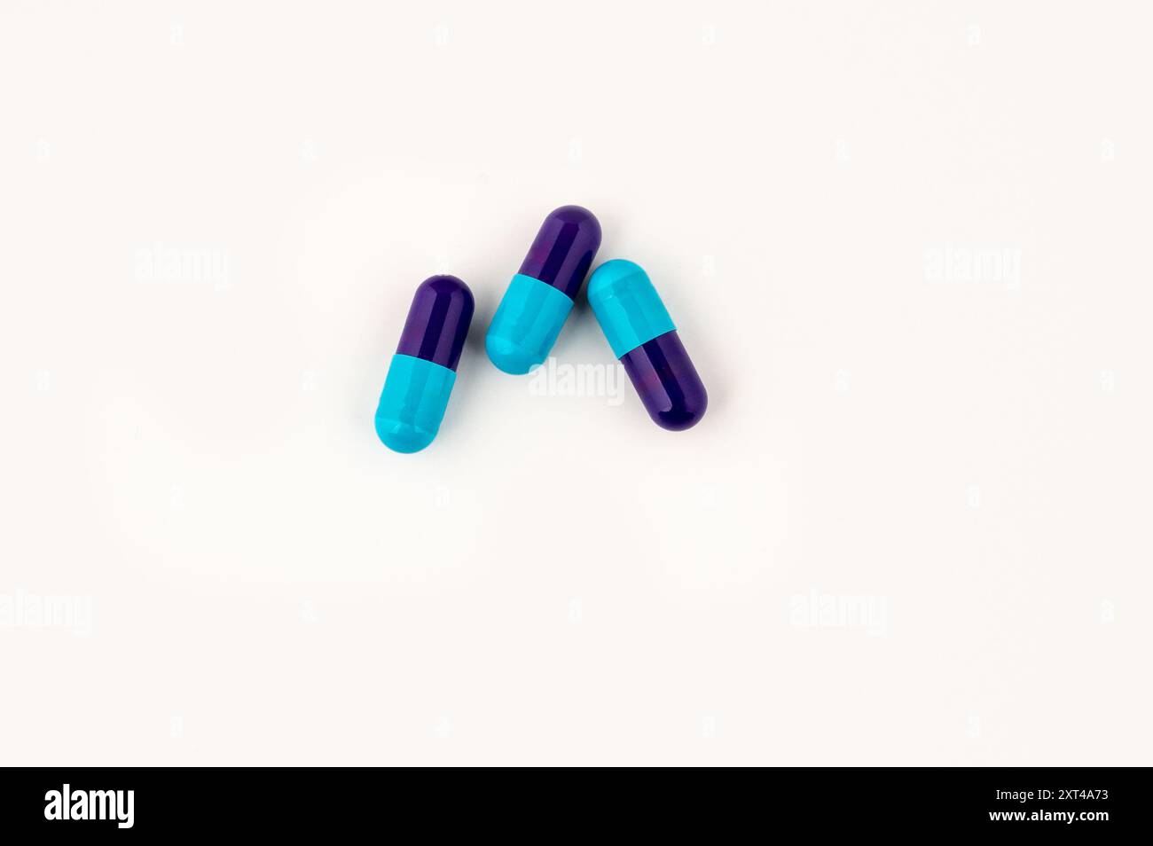 Concept - three light blue and dark blue capsule pills on white ...