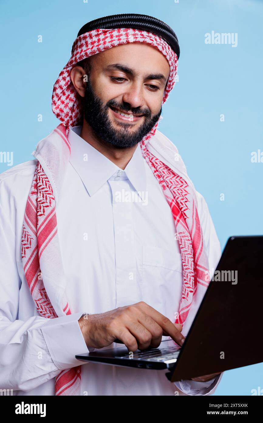 Smiling muslim man holding laptop and pressing button on keyboard with ...