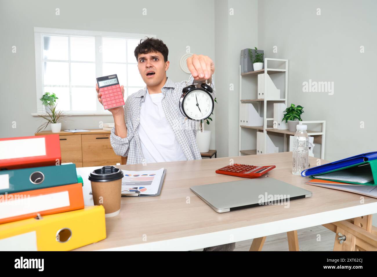 Shocked male accountant with calculator and alarm clock sitting at ...
