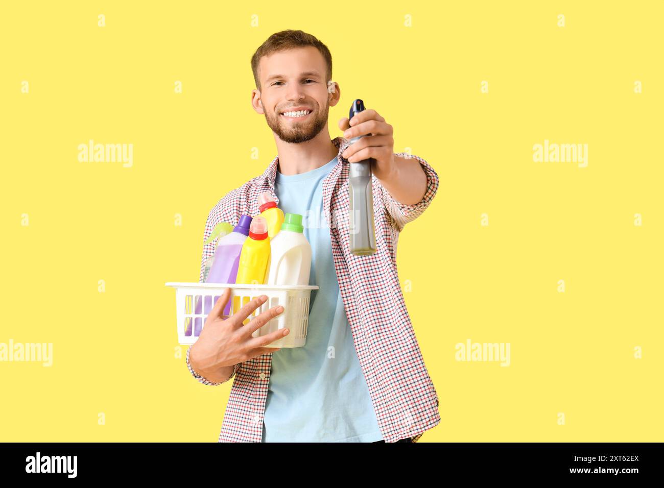 Male janitor holding basket with cleaning supplies on yellow background ...
