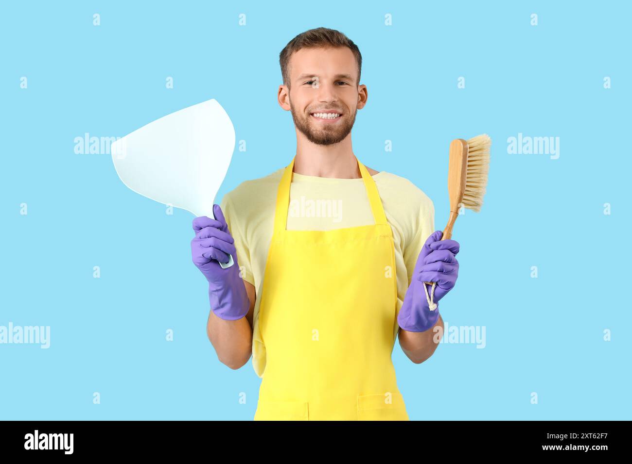 Male janitor in rubber gloves holding dust pan and brush on blue ...
