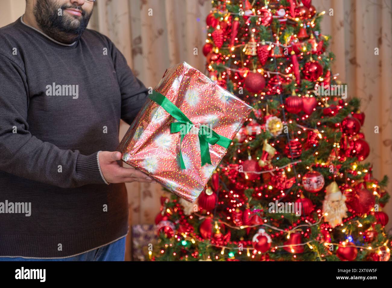 male holding gift box with christmas tree is behind him feeling excited ...