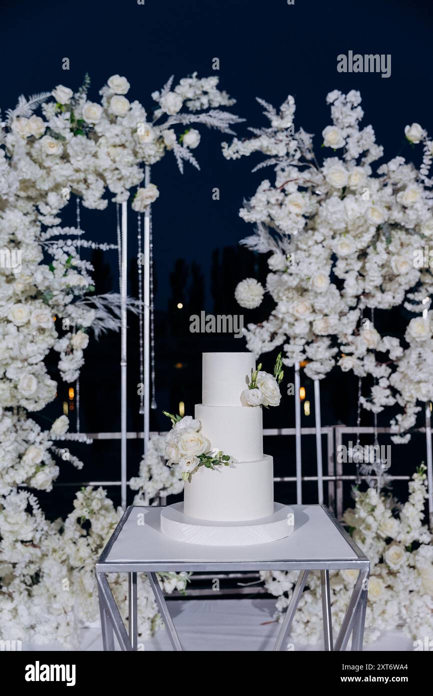 Wedding setup with three-tier white cake with floral accents. Wedding ...