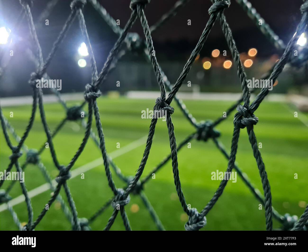 Blurred soccer field or pitch with artificial grass behind the mesh in ...
