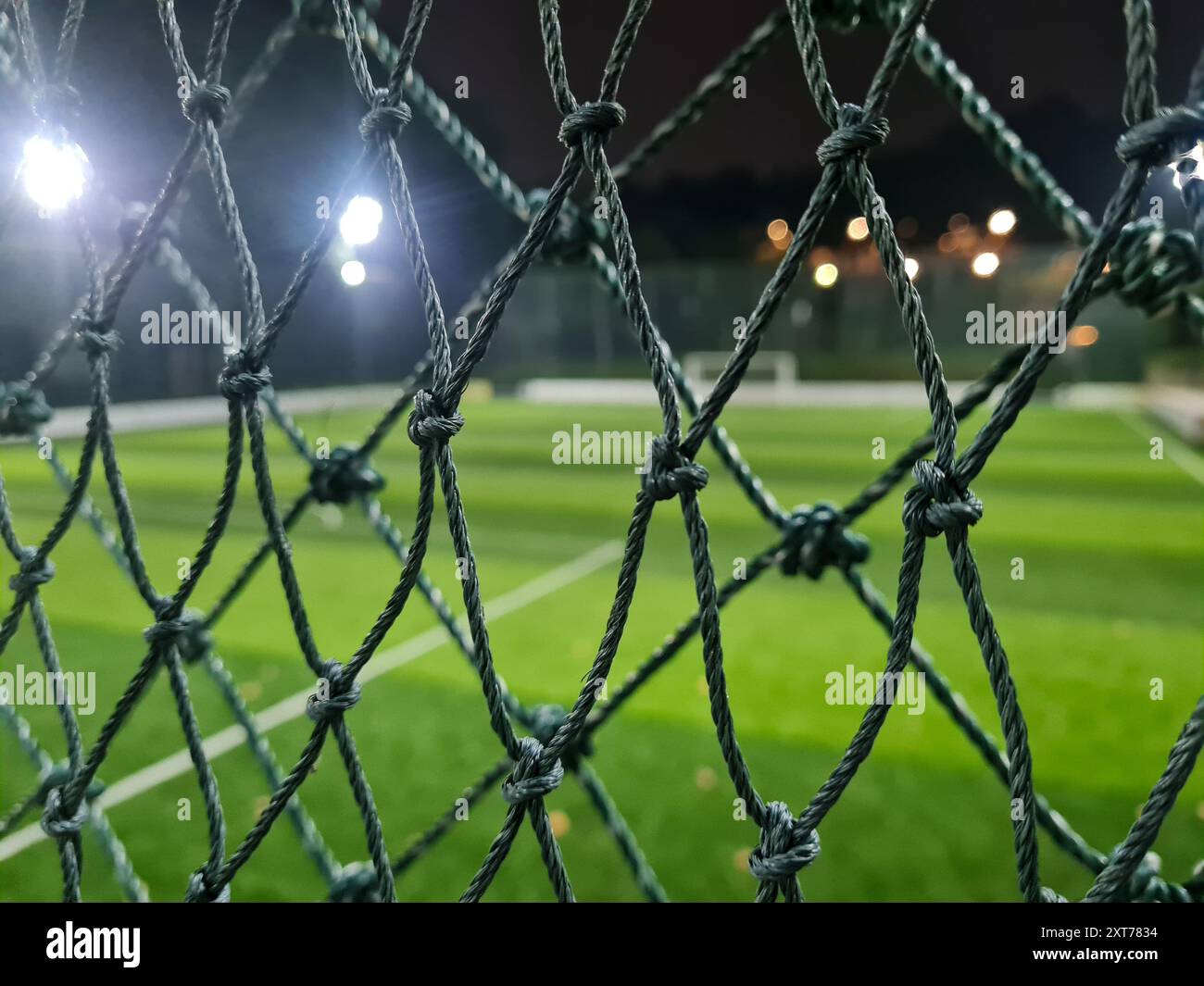 Blurred soccer field or pitch with artificial grass behind the mesh in ...
