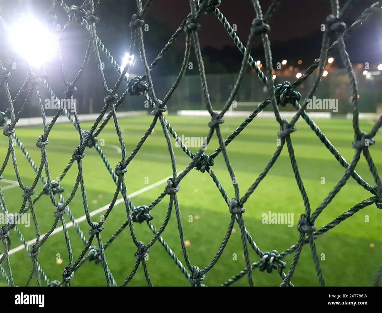 Blurred soccer field or pitch with artificial grass behind the mesh in ...