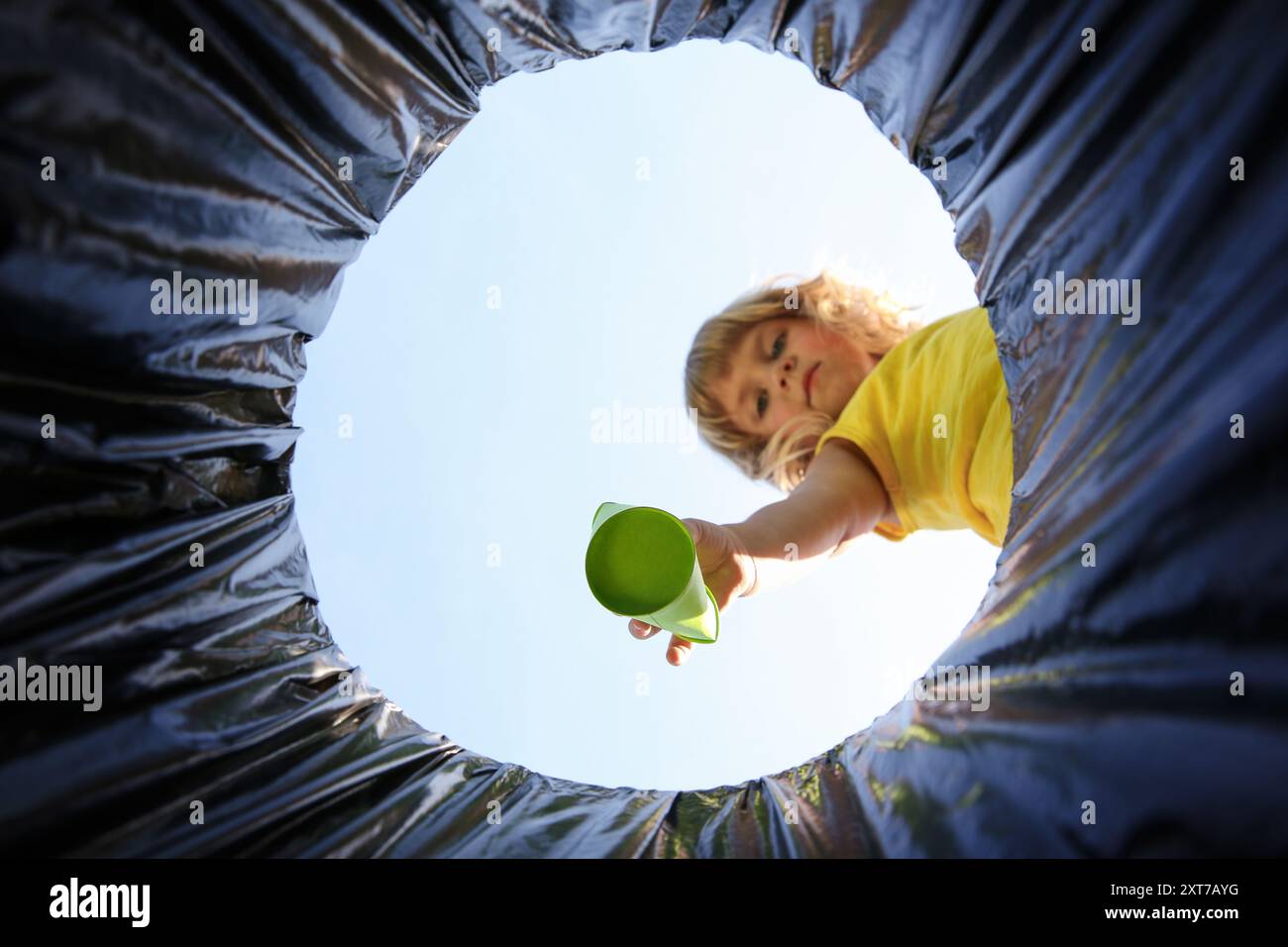 Cute little girl throwing garbage into trash bin outdoors, bottom view ...