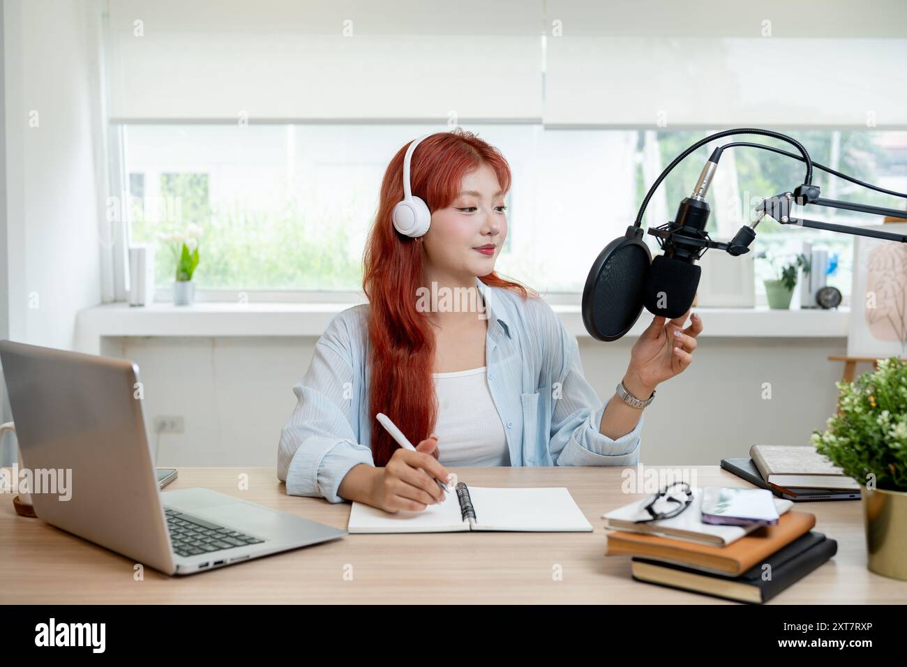 A beautiful Asian female podcaster with red curly hair is working in ...