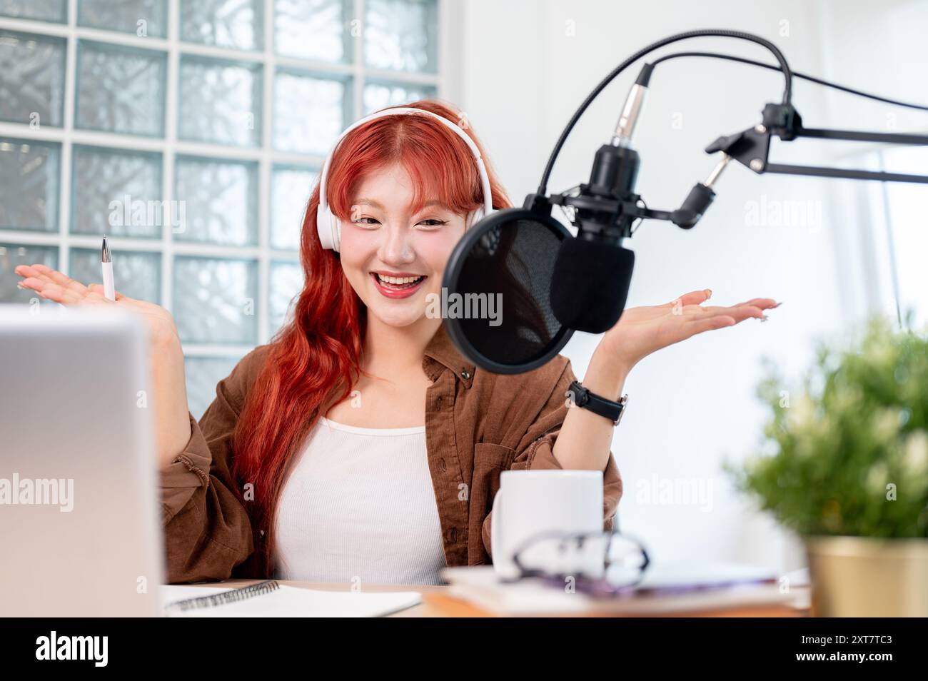 A beautiful and cheerful Asian female podcaster with red curly hair is ...