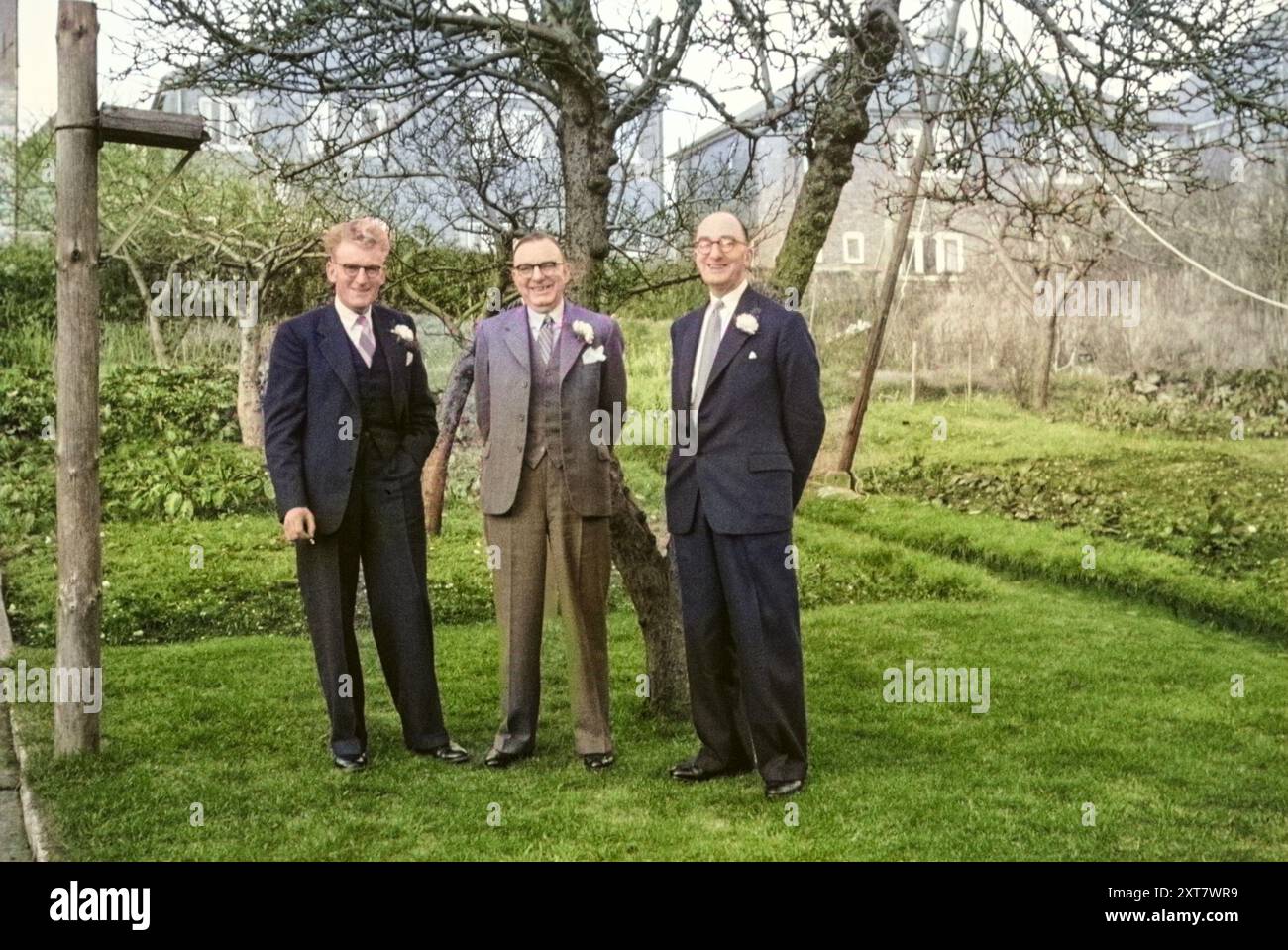 Three men in suits and white carnation buttonholes standing in garden ...