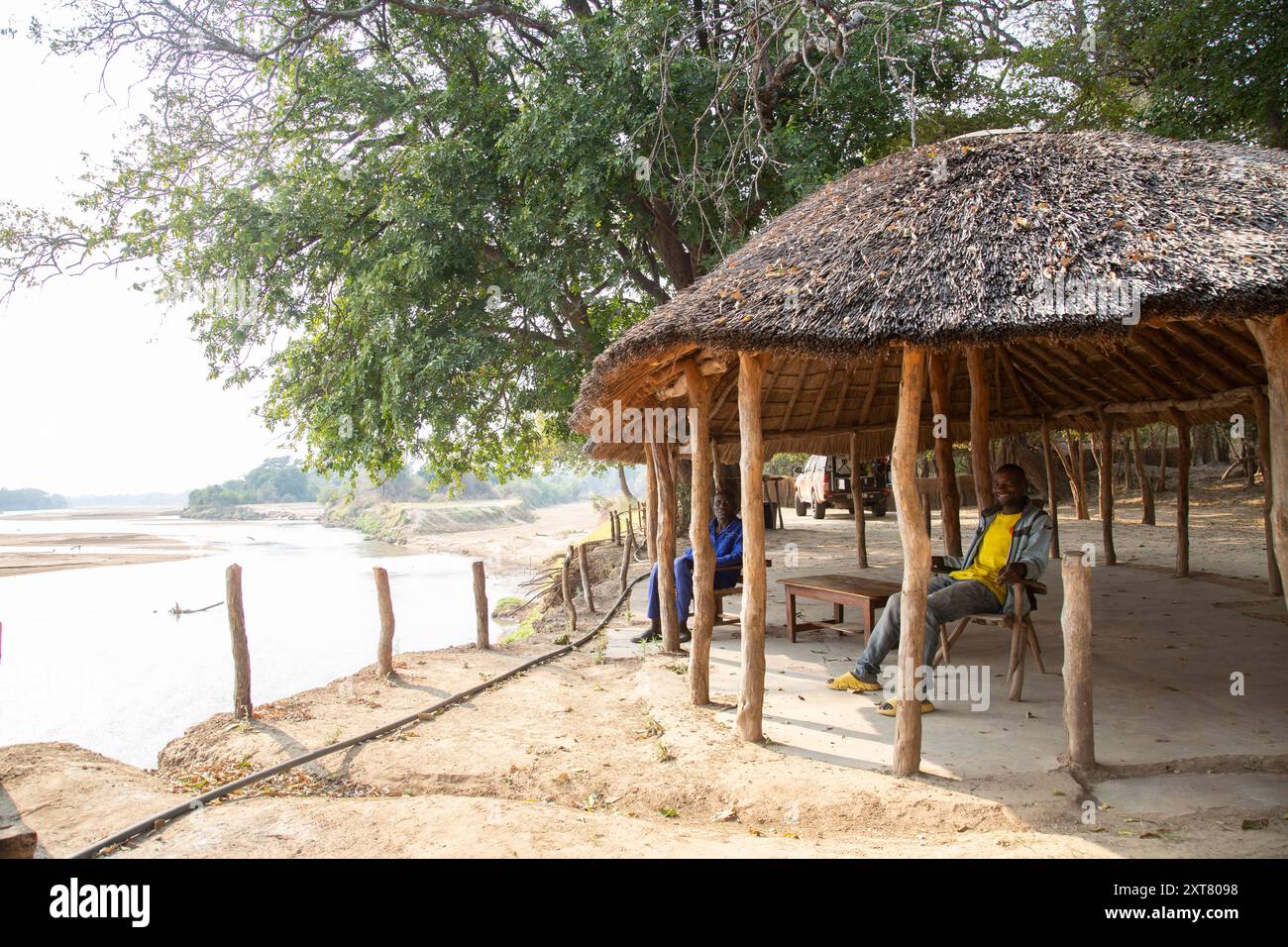 Smiling staff sit under a thatched area overlooking the Luangwa River ...