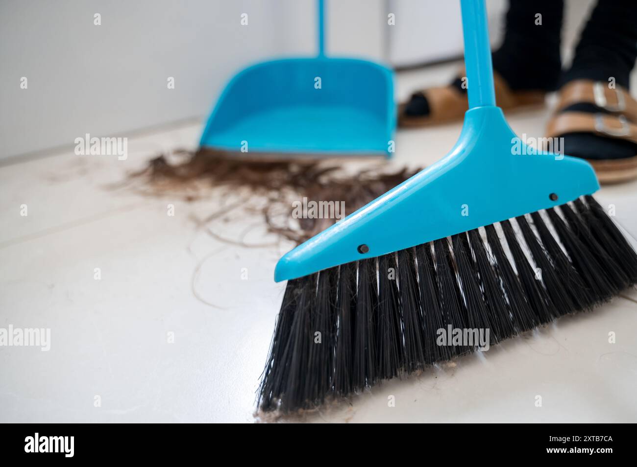 Hairdresser sweeps up freshly cut hair from salon floor using broom and ...