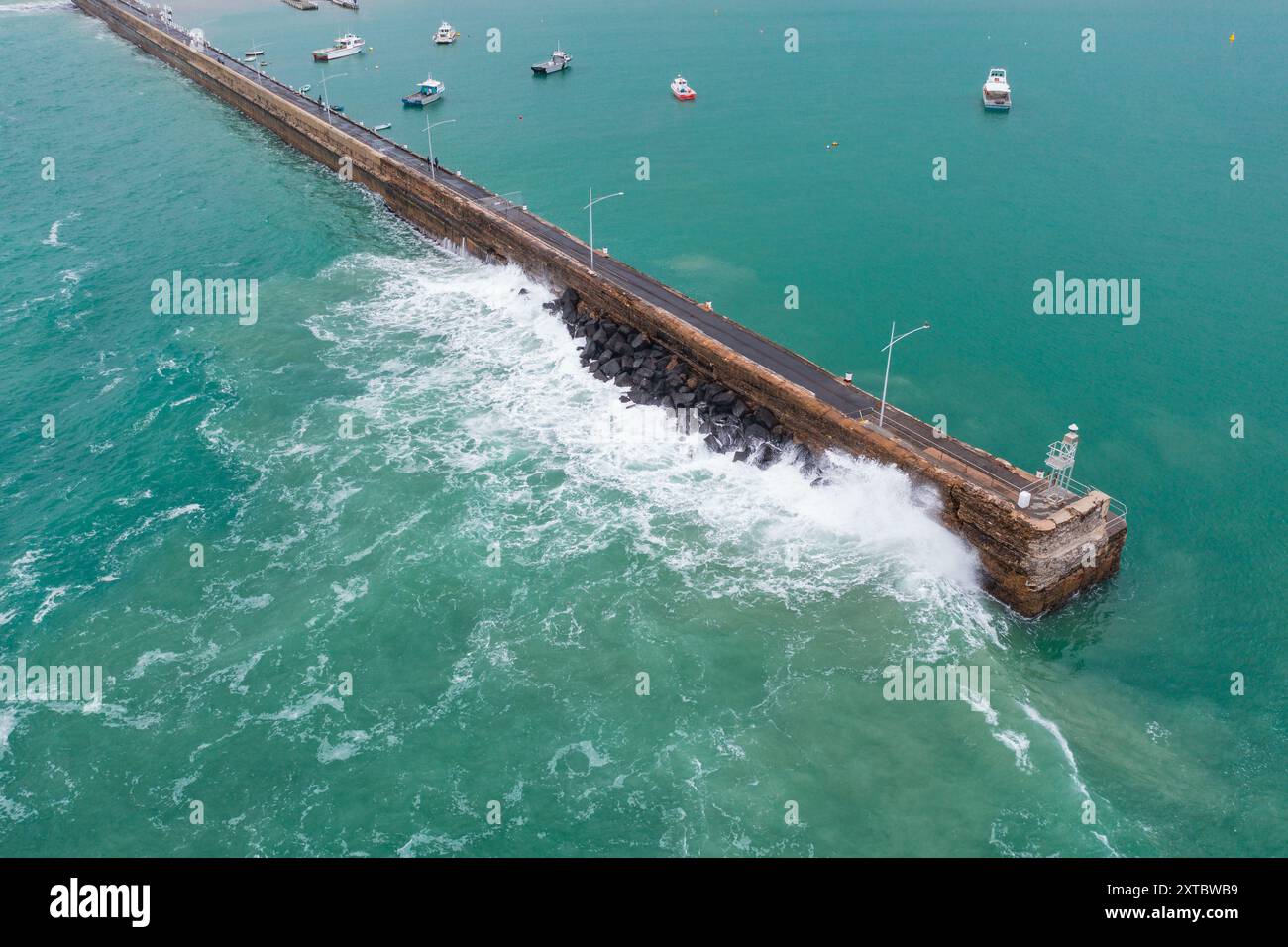 Aerial view of a large wave crashing onto a coastal breakwater at ...