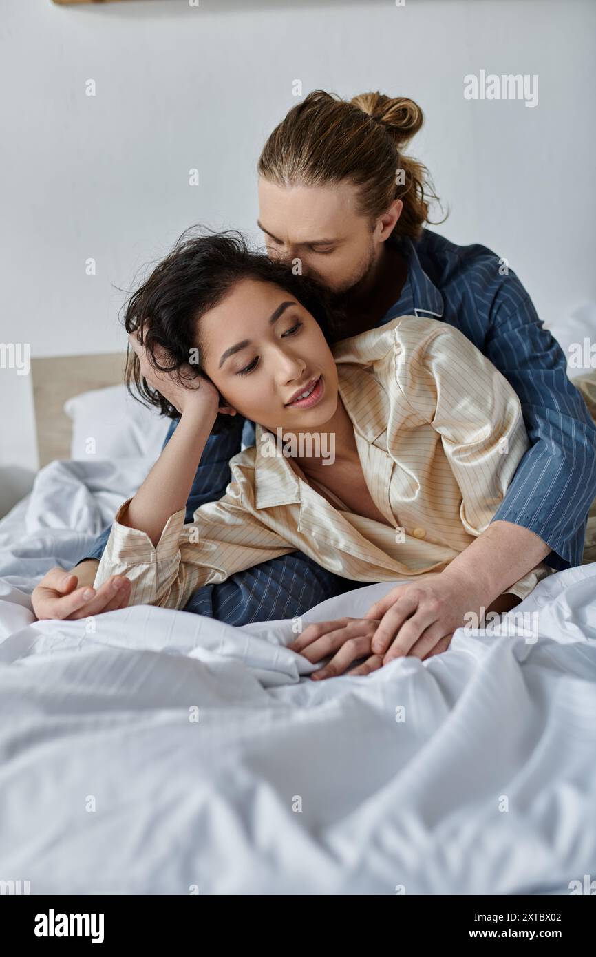 A loving couple cuddles in bed, the man gently kissing his partners ...