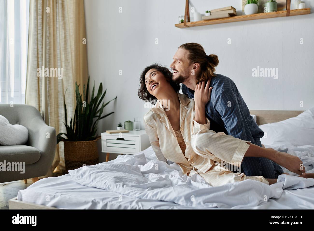 A loving couple shares a laugh and a hug on their bed, enjoying a ...
