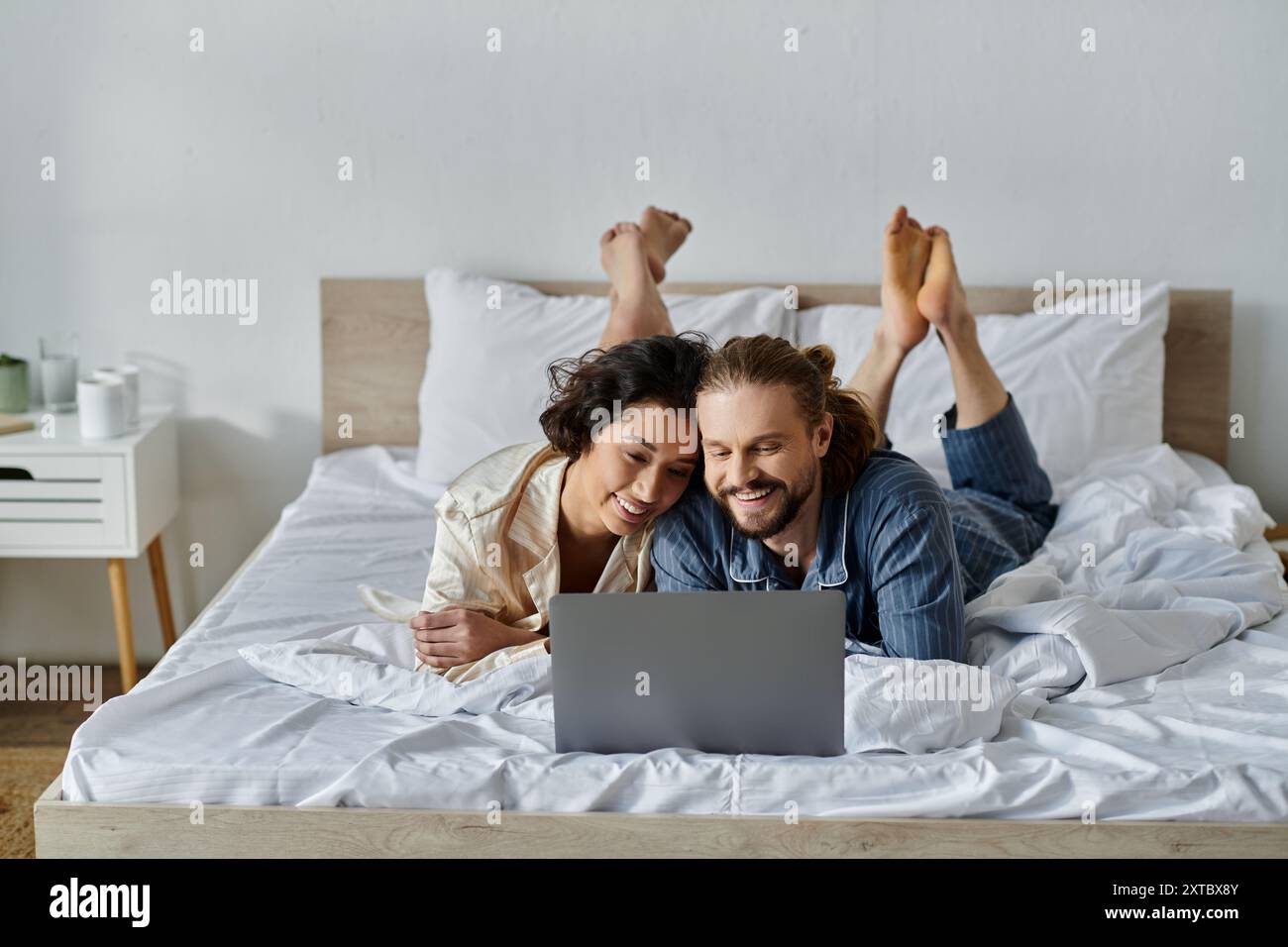A loving couple cuddles in bed, sharing a laptop as they browse the ...