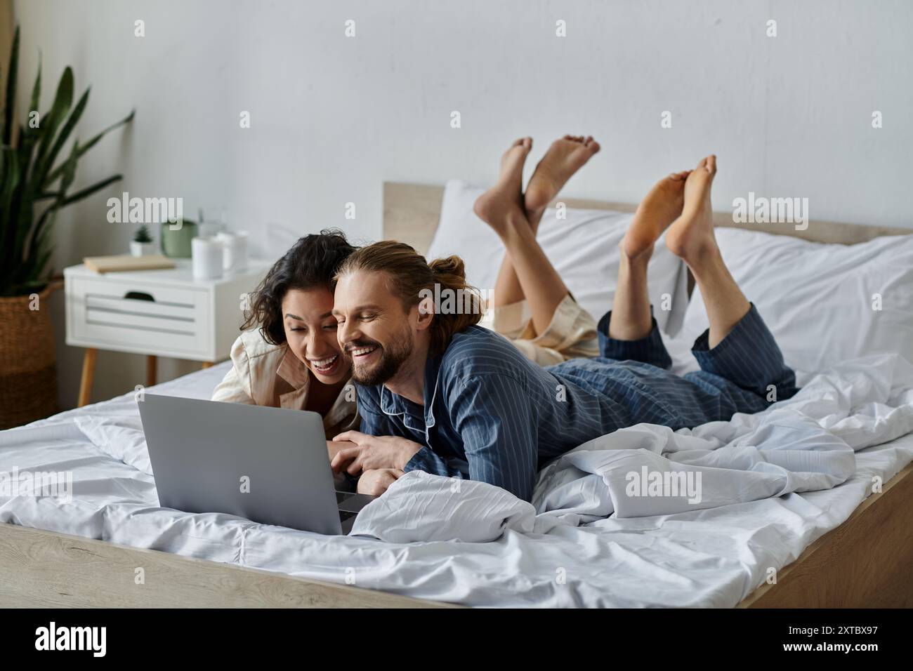 A loving couple cuddles in bed, sharing a laugh while browsing the ...