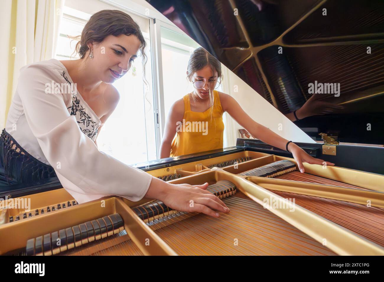 Female piano teacher teaching teenage girl student the inner workings ...