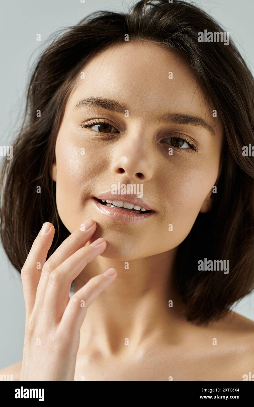 A woman with dark hair poses against a light background, her hand ...