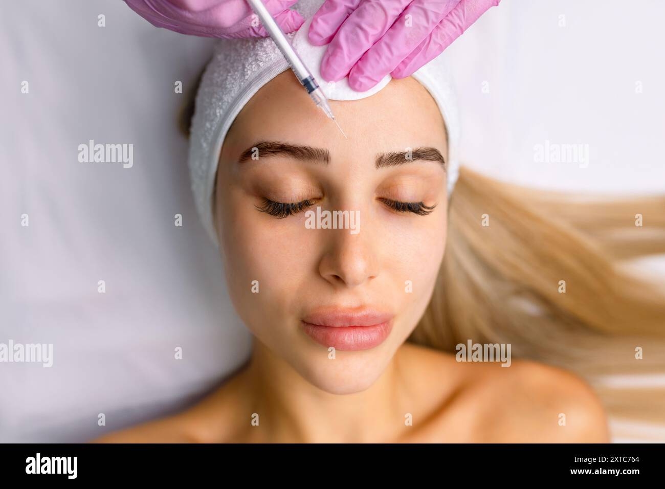 Close up of hands of young cosmetologist injecting botox in female face ...