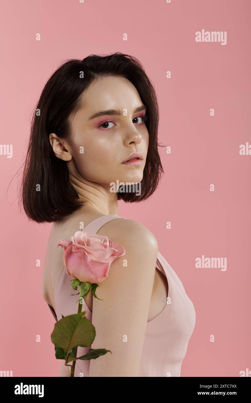 A woman with short dark hair poses with a pink rose against a pink ...