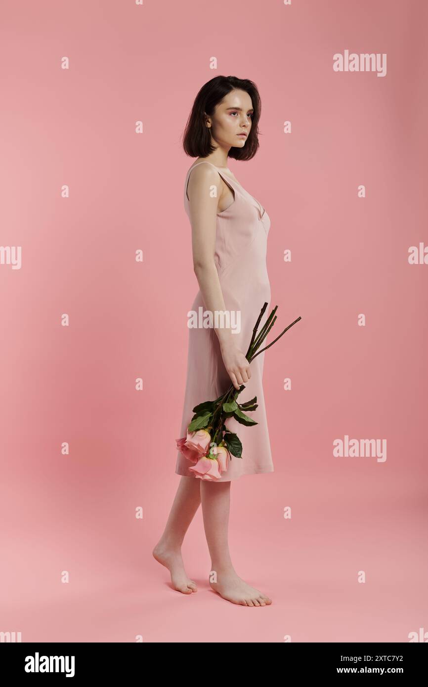 A woman in a pink dress poses gracefully with a bouquet of roses ...