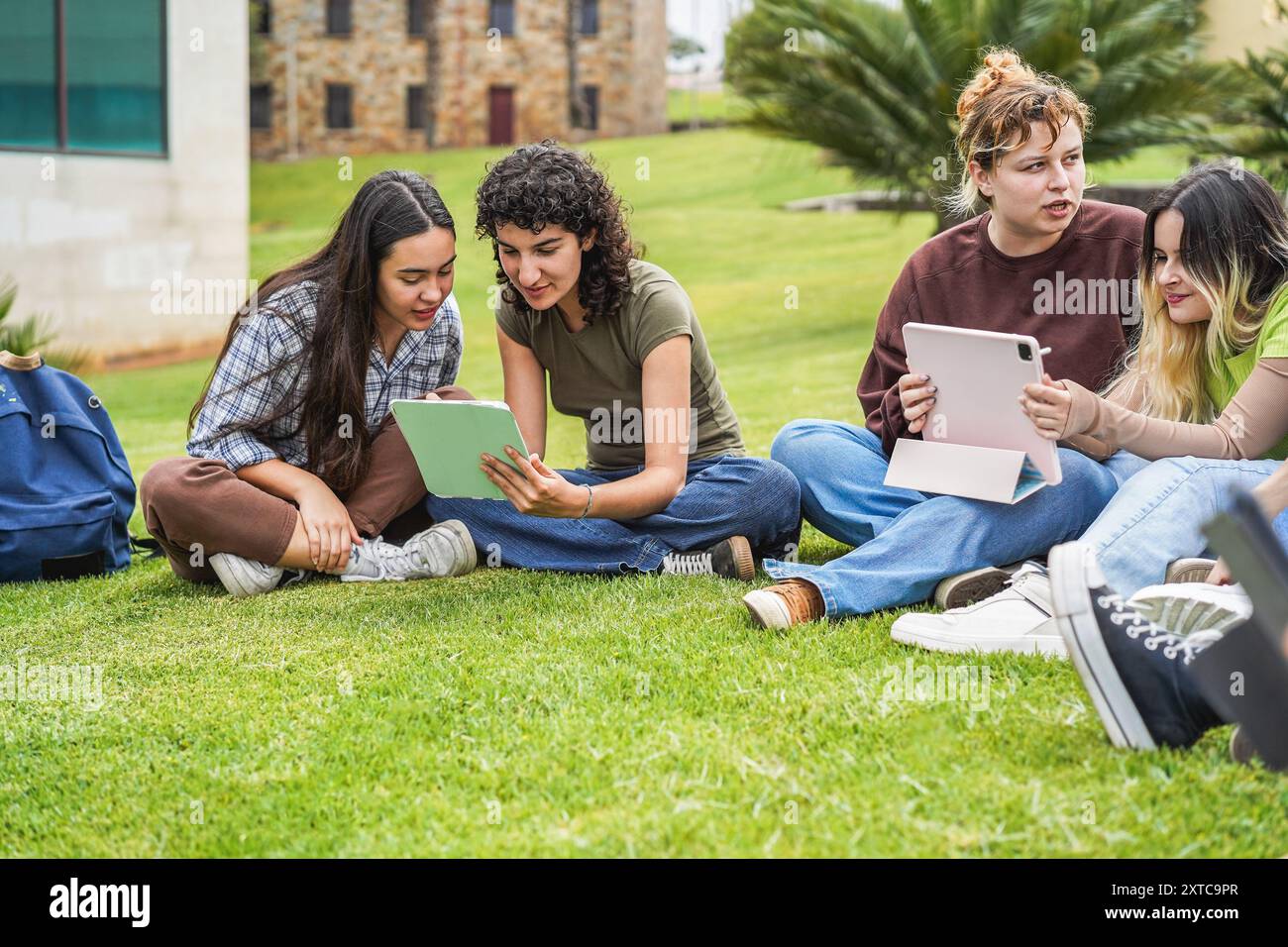 Caucasian students studying with digital tablets sitting on grass at ...
